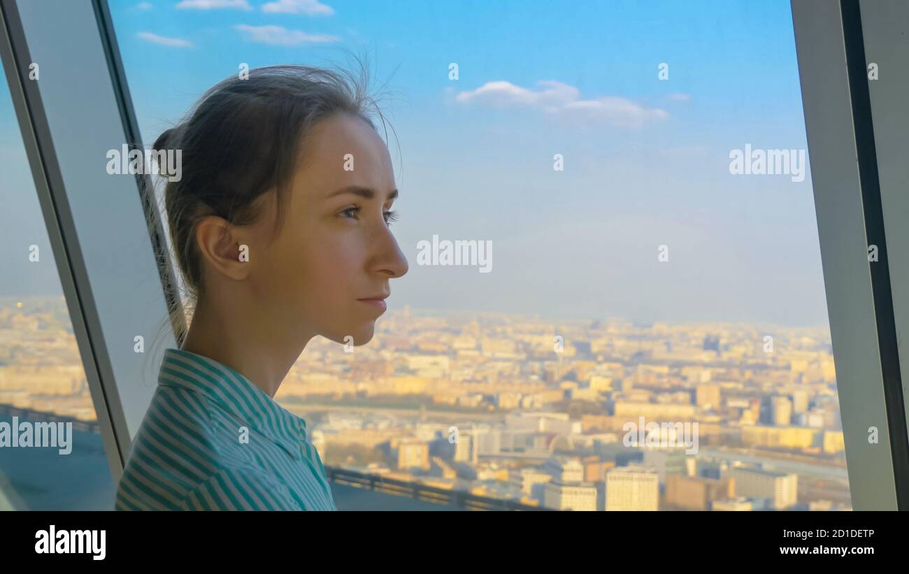 Portrait of woman looking at cityscape through window of skyscraper ...