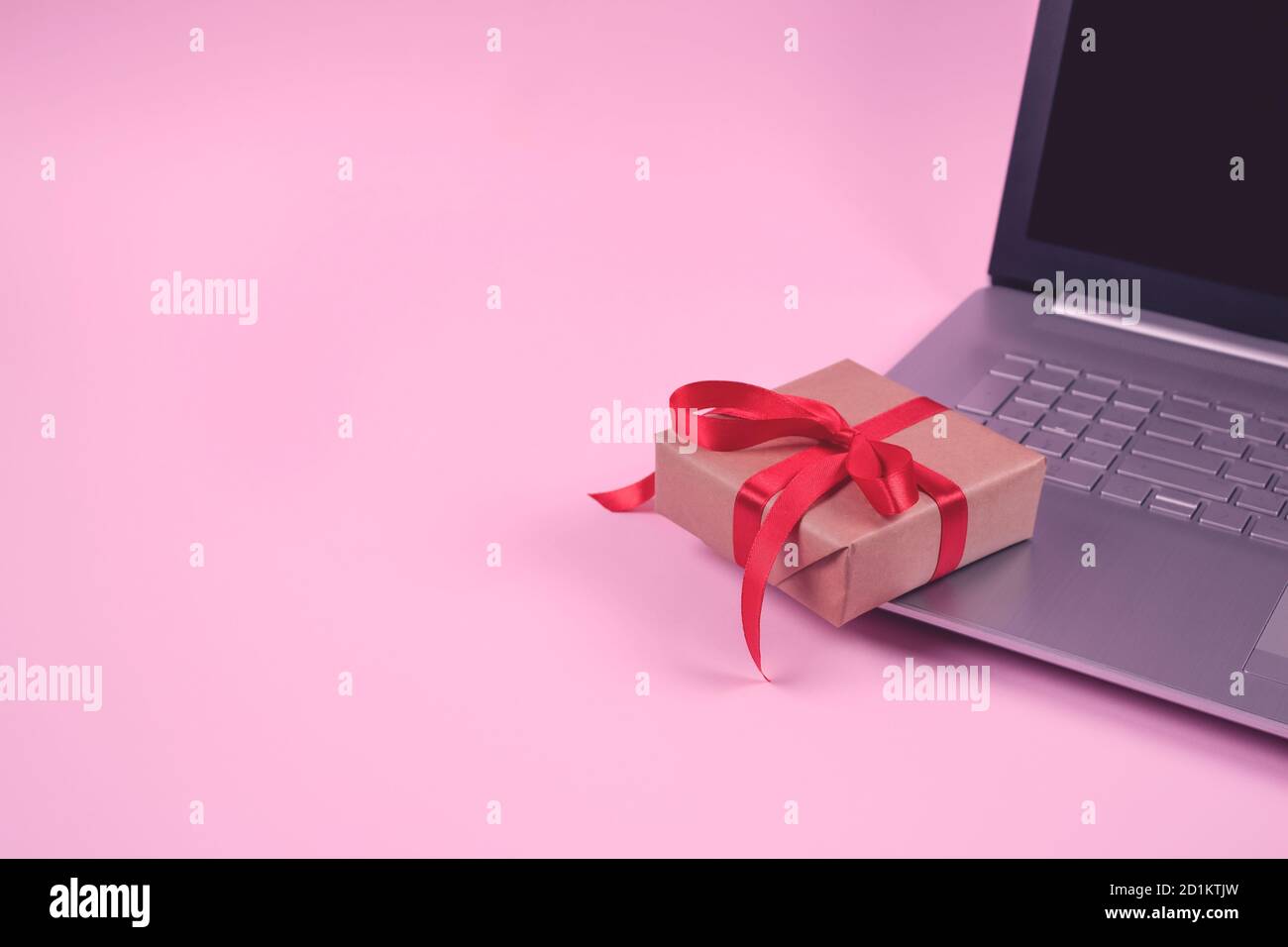 Front view on laptop computer and present box with red bow on pastel ...