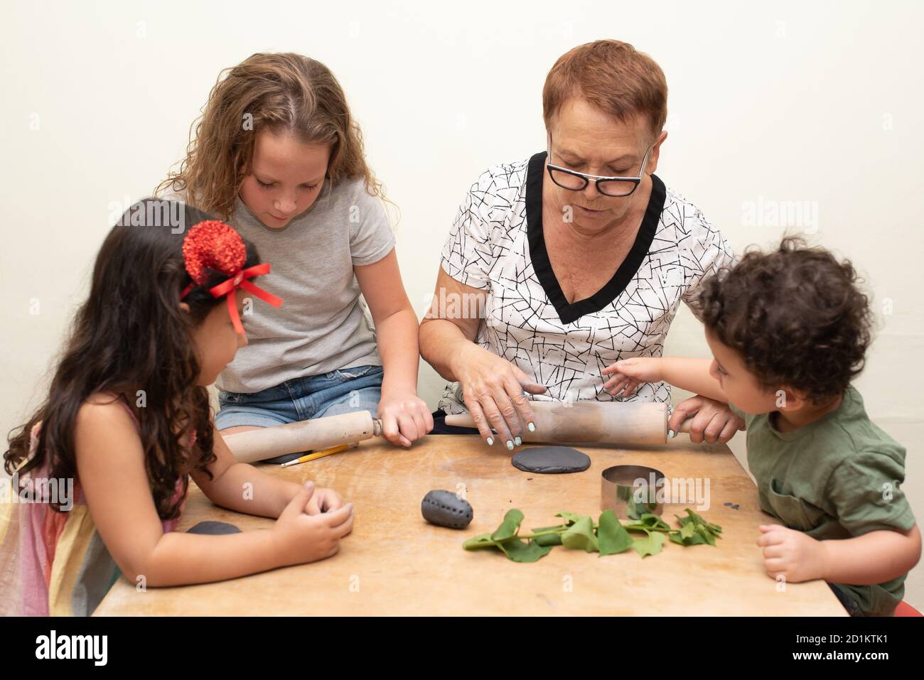 A Senior Woman Is Teaching A Little Kids How To Form With Clay ...