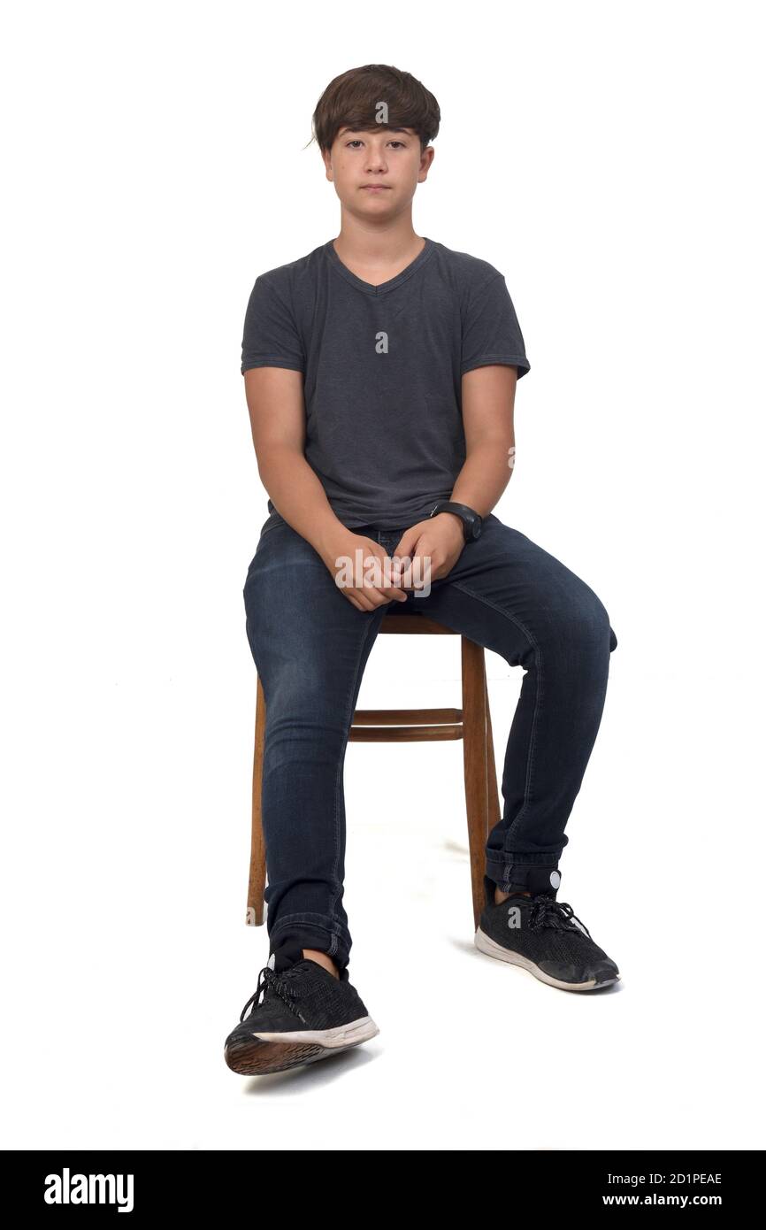 front view of teenage boy sitting on a chair with white background ...