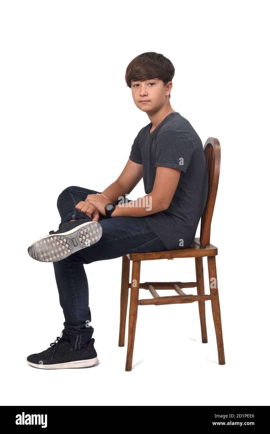 side view of teenage boy sitting on a chair with white background, legs ...