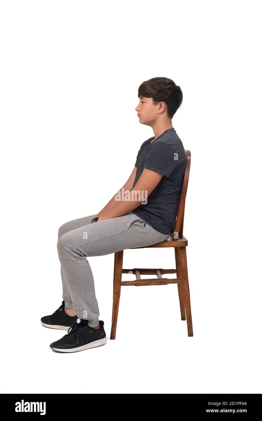 side view of teenage boy sitting on a chair with white background ...