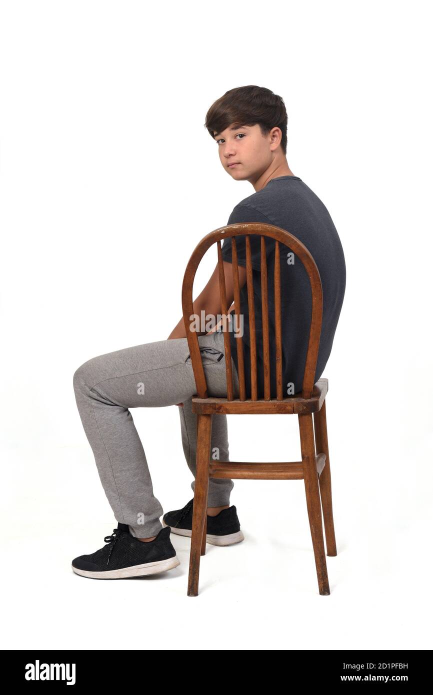 side view of teenage boy sitting on a chair with white background ...
