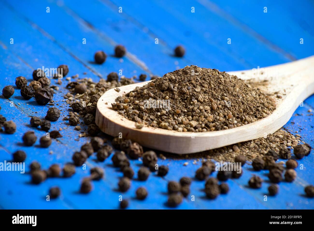 Close-up of black pepper powder in wooden spoon and black peppercorns ...