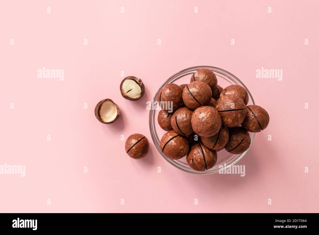 Raw macadamia nuts in a transparent glass bowl on pink solid background ...