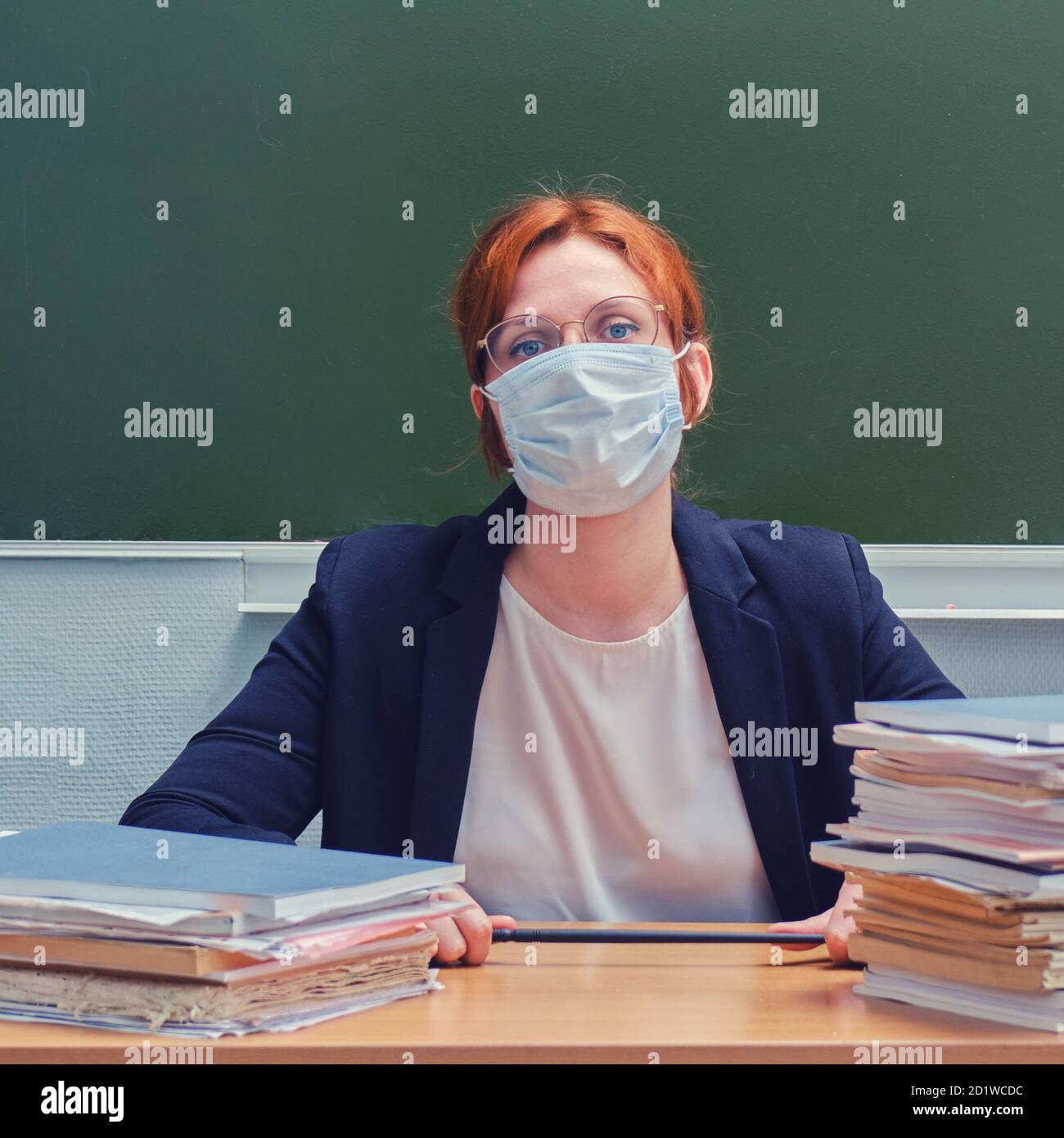 Woman teacher sitting in a medical mask at a school desk, close up. Sad ...