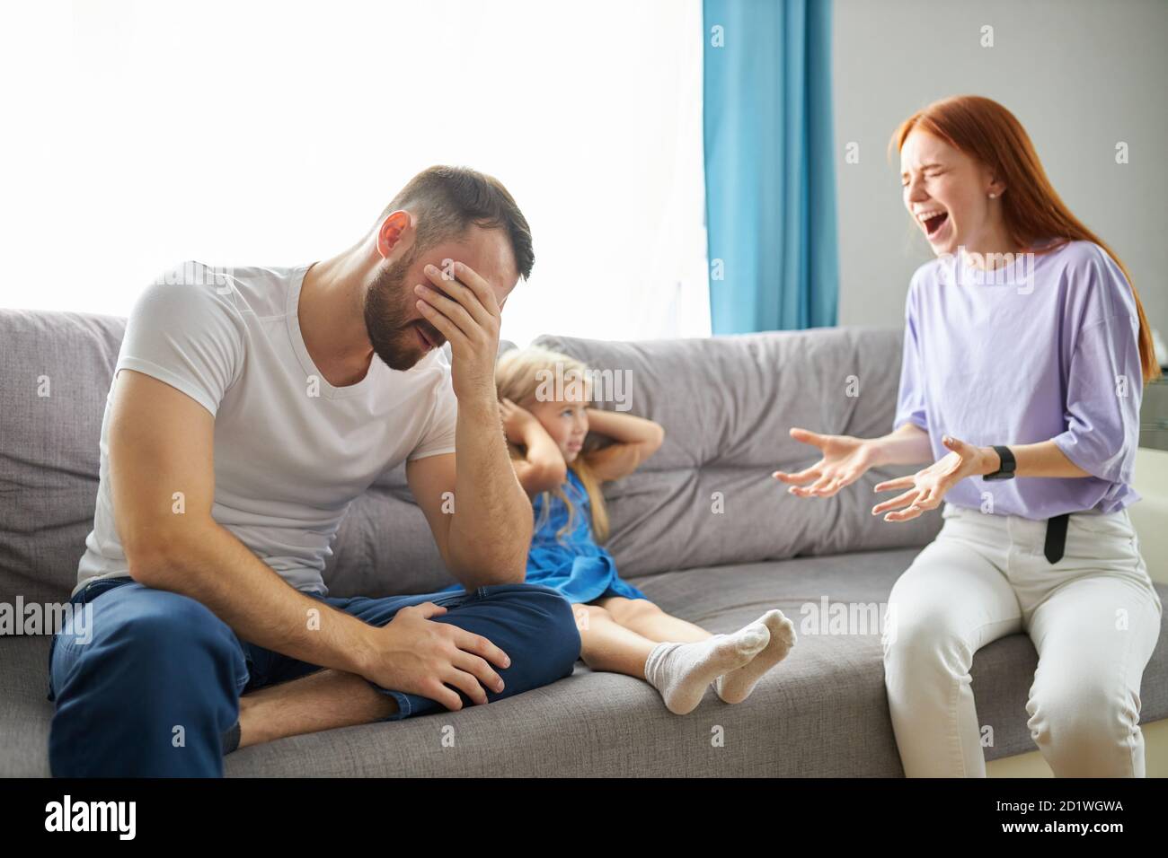 sad, desperate little girl during parents quarrel, she clog the ears sitting on sofa at home ...