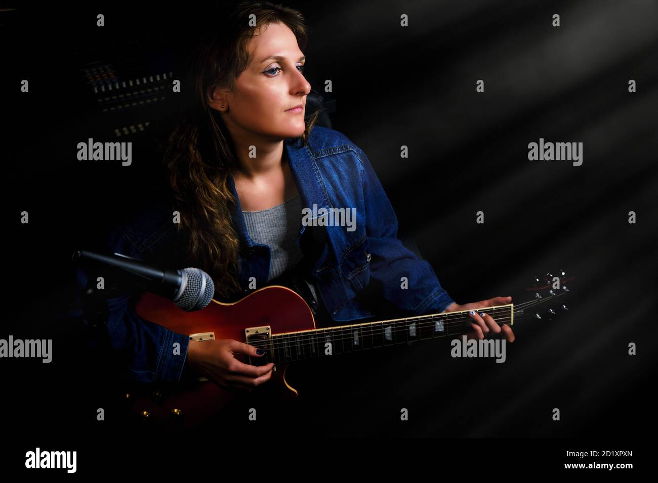 Woman with a red electric guitar in a denim jacket records a song at a ...