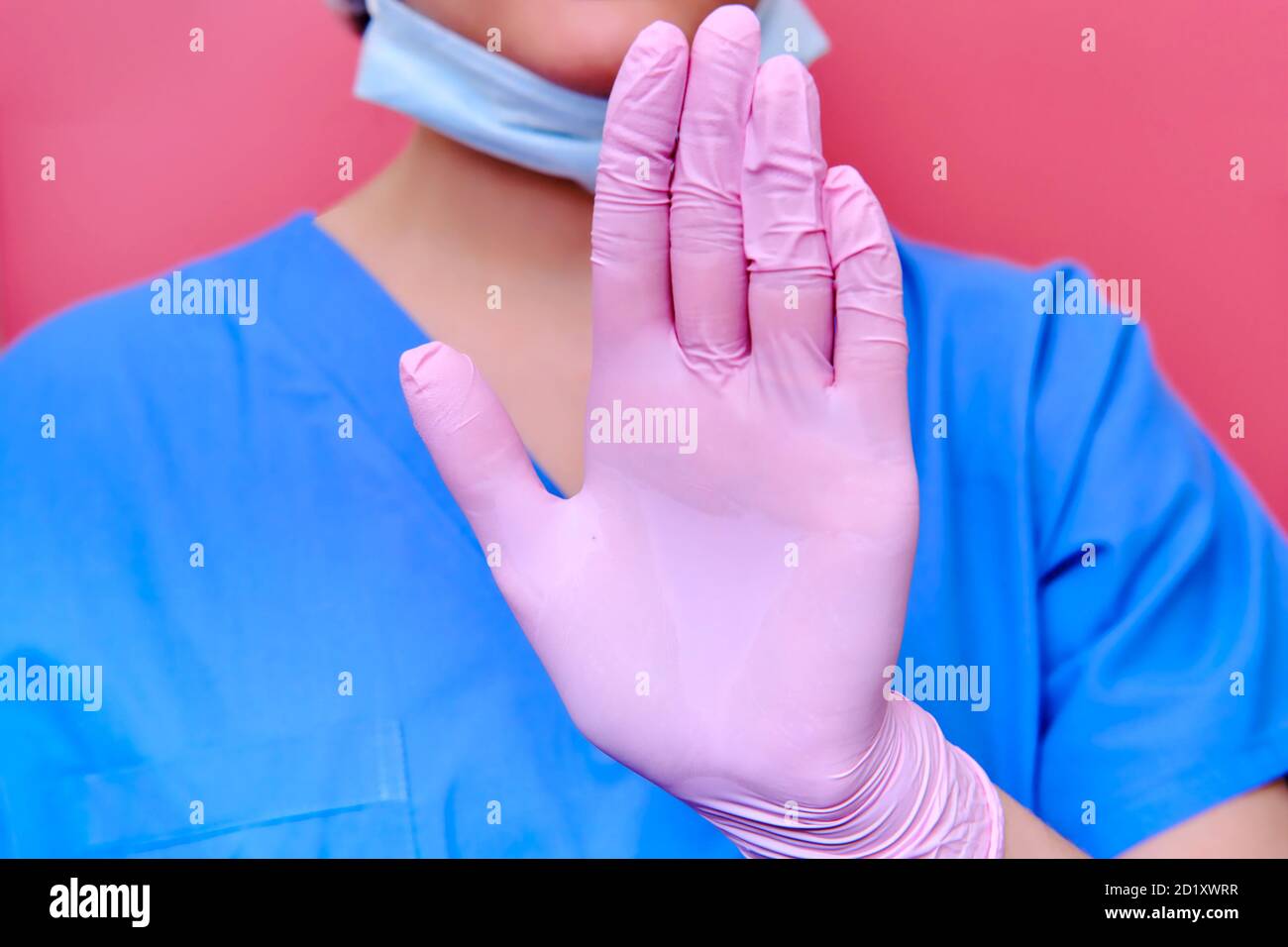 A doctor in a blue uniform on a pink background shows a stop gesture ...