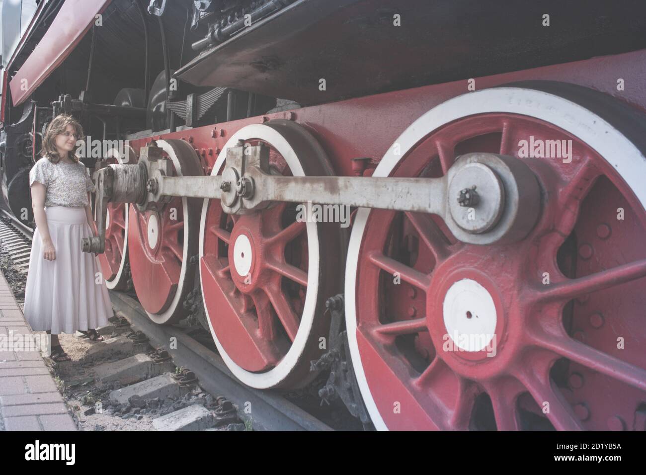 The girl looks at the big wheel train. Vintage steam train stands on ...
