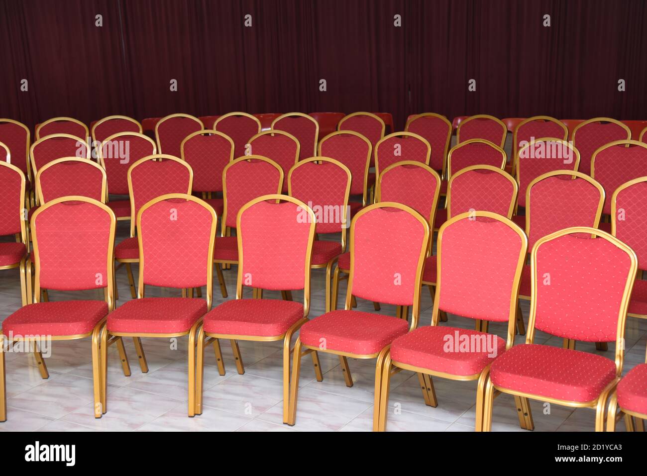 Red colored chairs with gold colored metallic frame arranged in ...