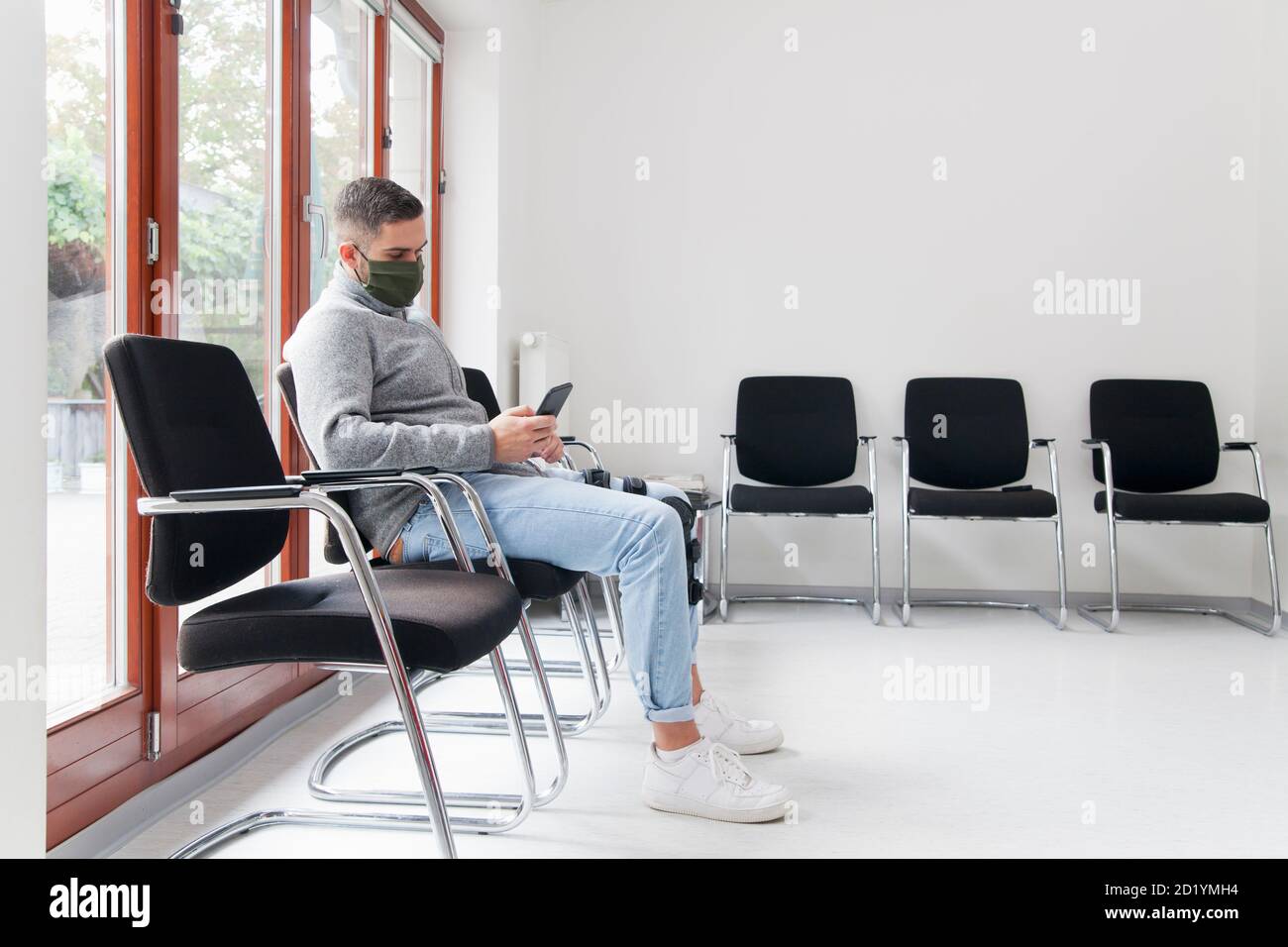 Young man with face mask sitting in a waiting room of a hospital or ...