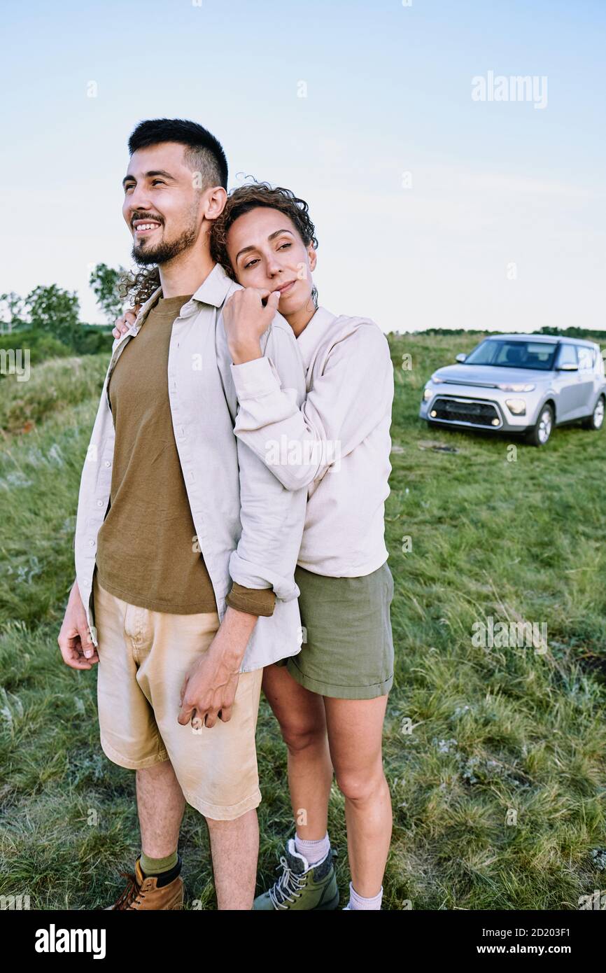 Happy contemplative girl looking into distance and embracing boyfriend ...