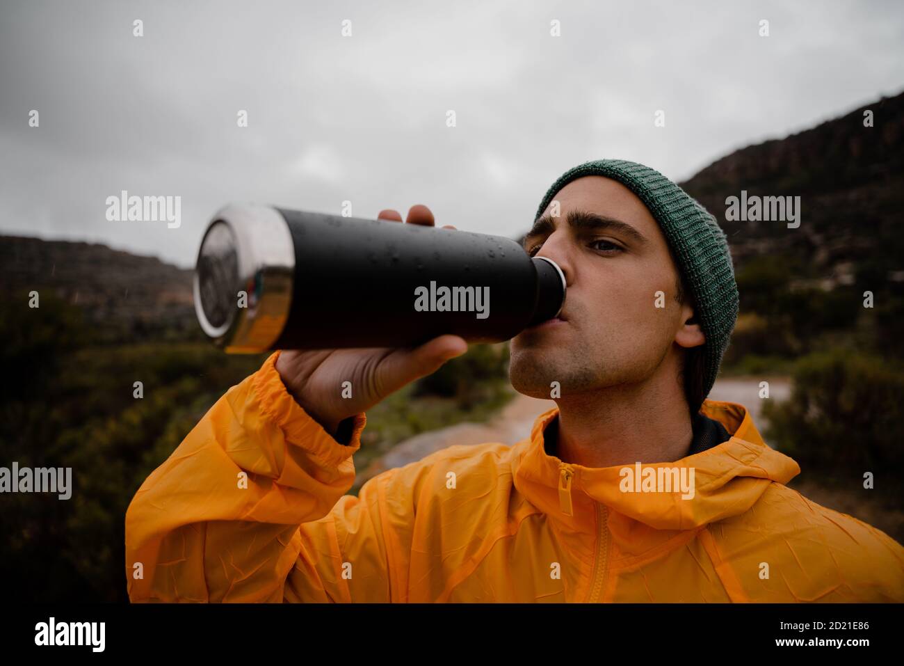 Tired young male trail runner drinking water from reusable bottle after ...
