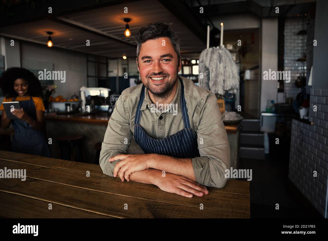 Handsome coffee shop owner smiling while sitting at table in funky ...