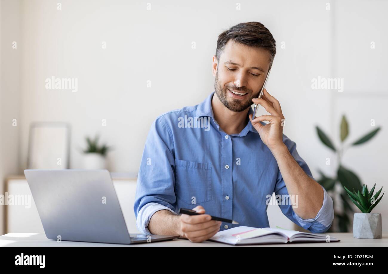 Smiling Businessman Taking Notes While Having Phone Conversation In ...