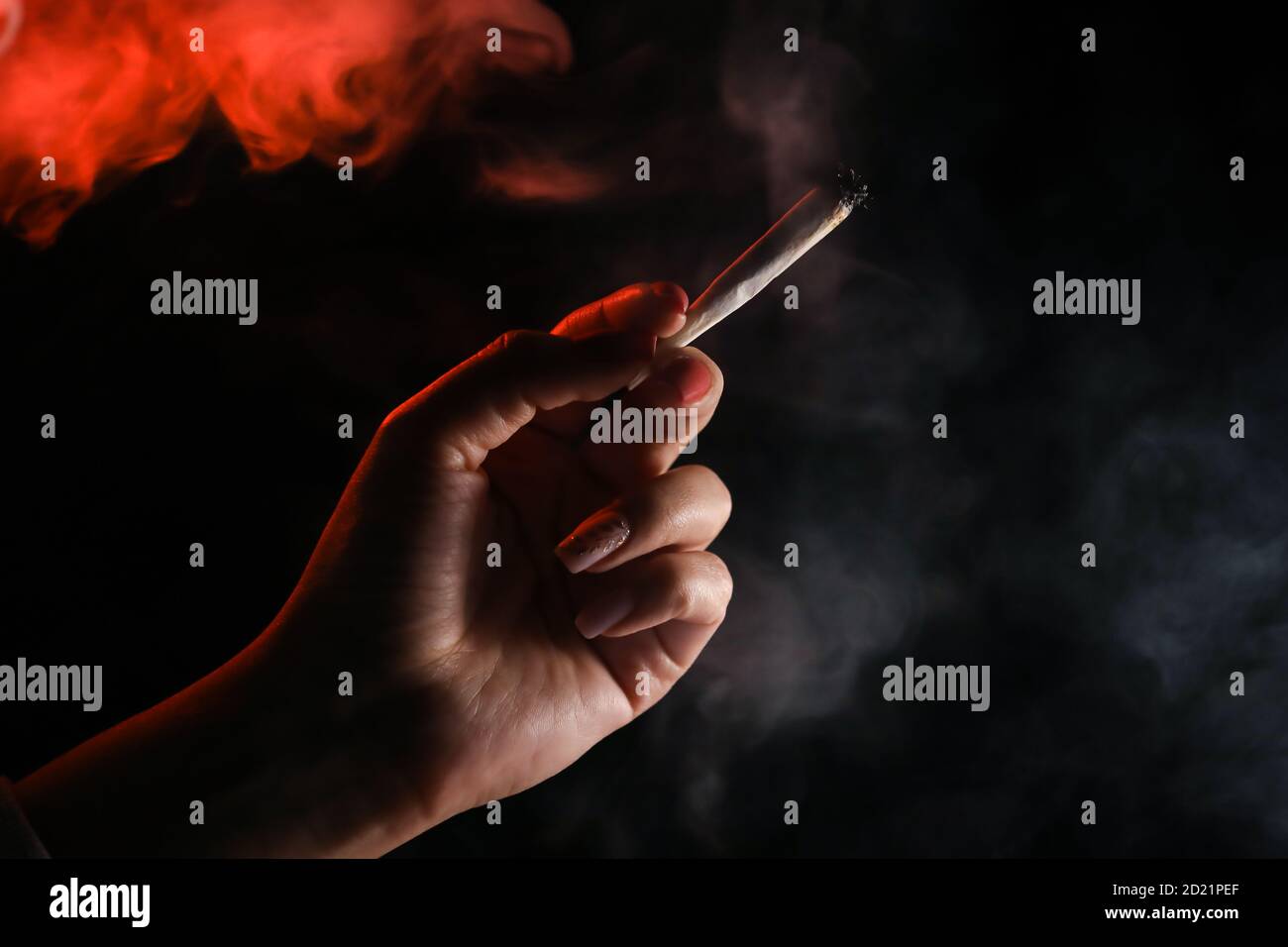 Woman hand holding cigarette in a smoke against black background ...