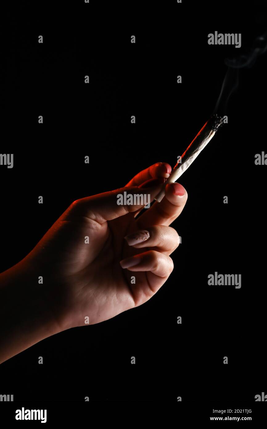 Woman hand holding cigarette in a smoke against black background ...