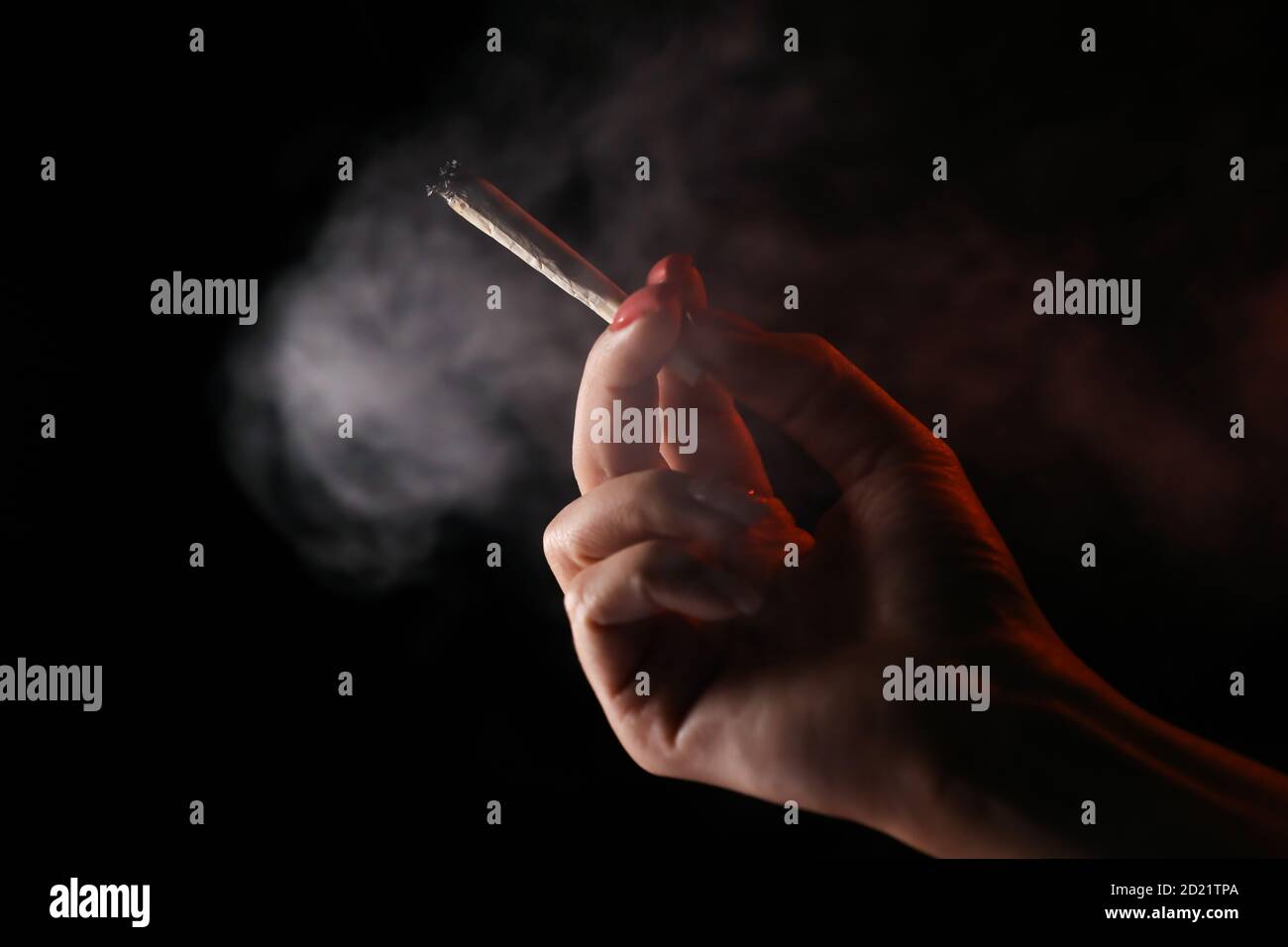 Woman hand holding cigarette in a smoke against black background ...