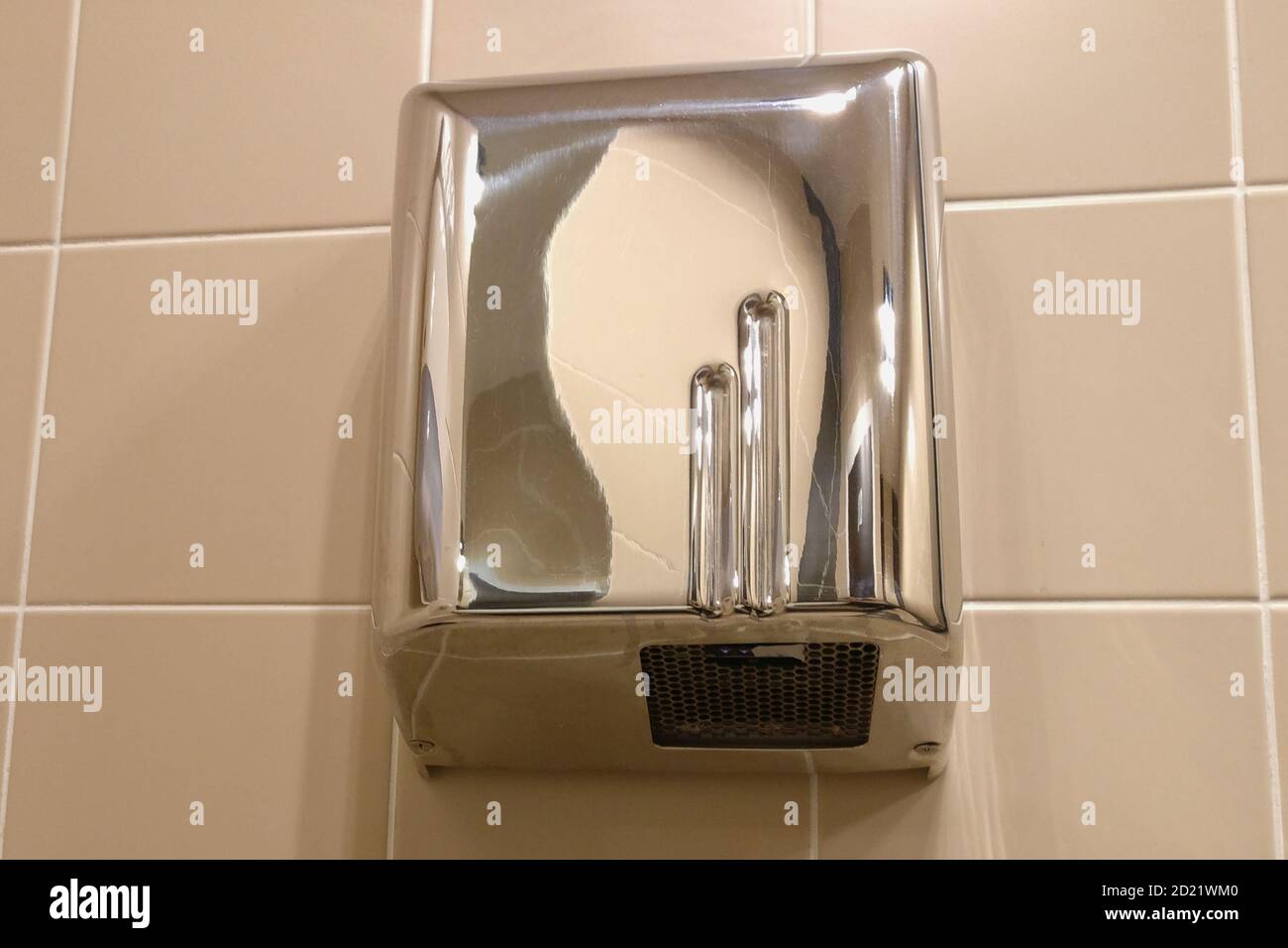 Metal hand dryer on the tiled wall. Hot air for drying hands on the ...
