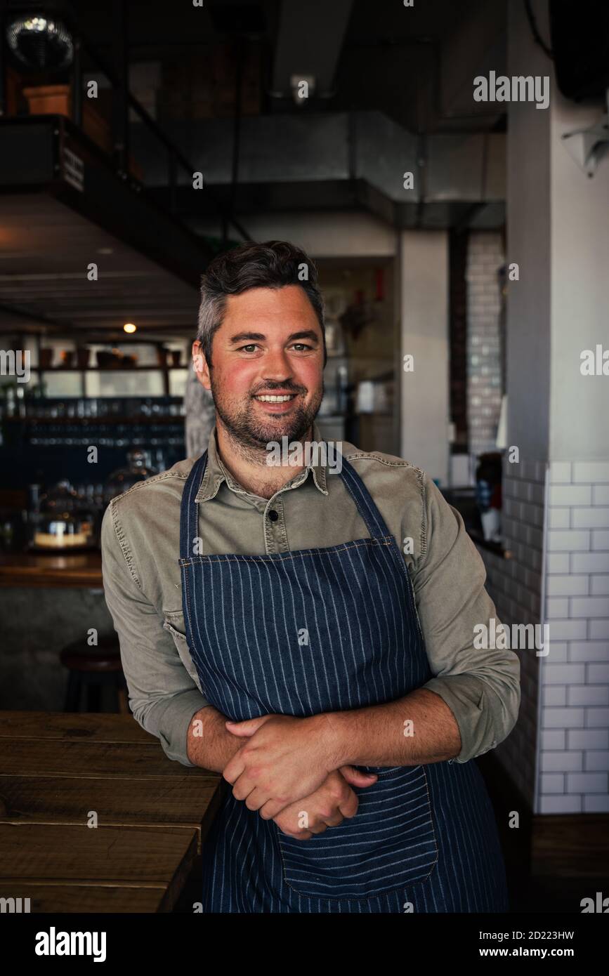 Tanned male owner smiling while leaning against bench with crossed ...