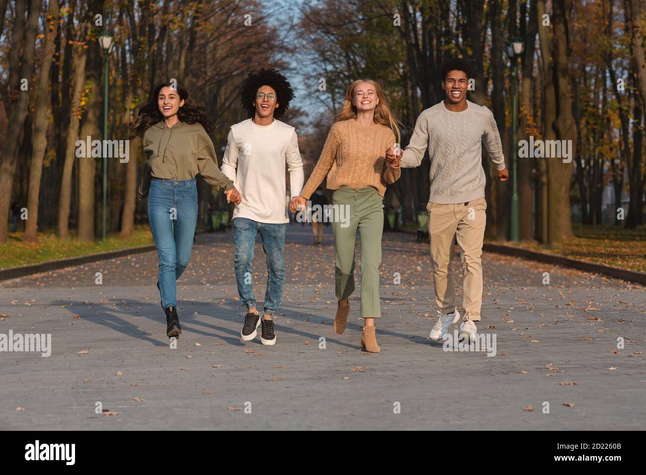Cheerful friends holding hands and running by park Stock Photo - Alamy