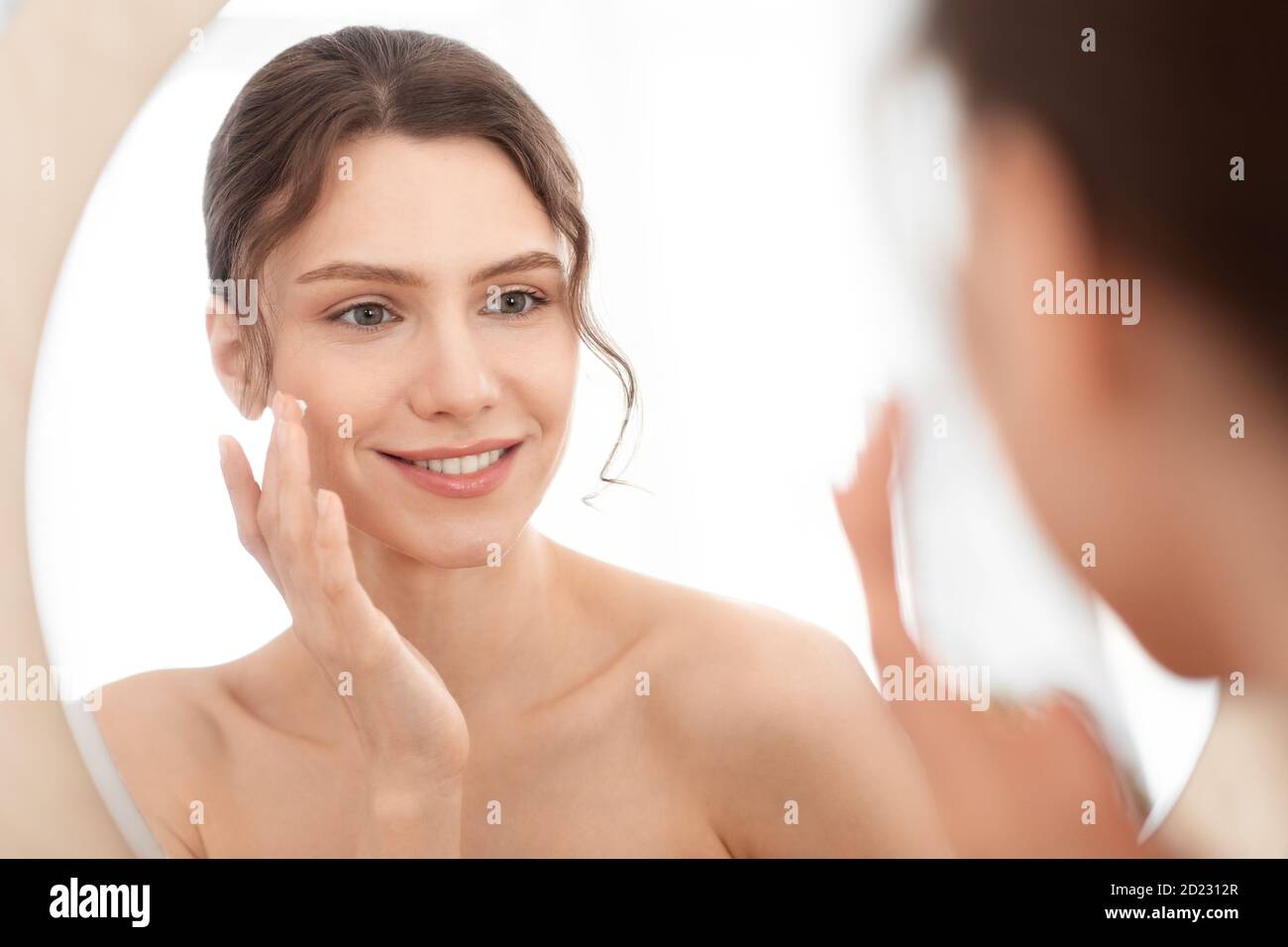 Cheerful pretty young lady using face cream Stock Photo - Alamy