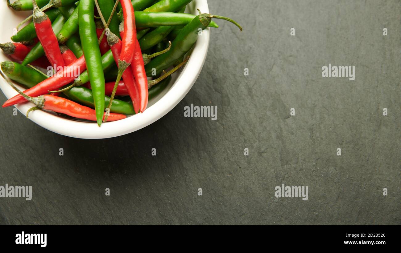 Assorted Chilli peppers in a white ceramic bowl on a natural slate ...