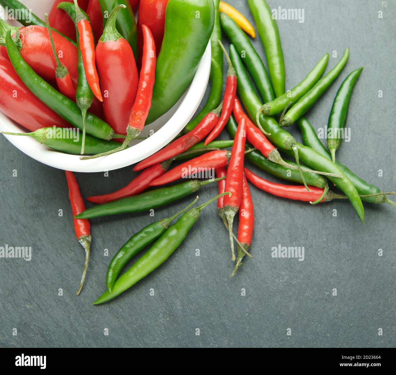 Assorted Chilli peppers in a white ceramic bowl on a natural slate ...