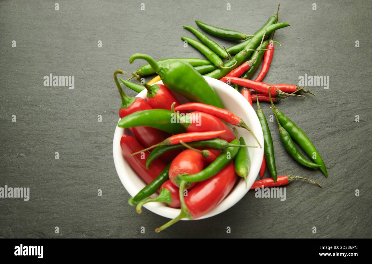 Assorted Chilli peppers in a white ceramic bowl on a natural slate ...