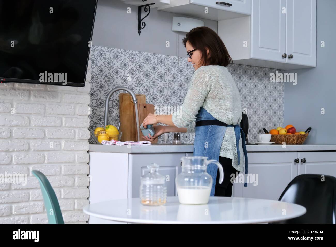 Homework in kitchen, woman housewife in an apron washes cup Stock Photo ...