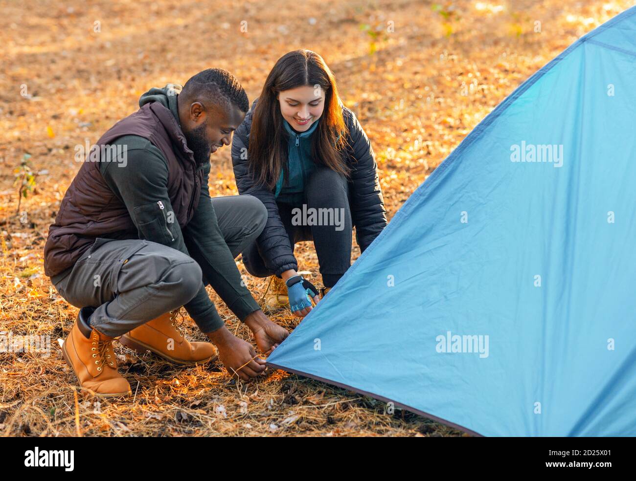 Multiracial young couple setting tent, camping together Stock Photo - Alamy