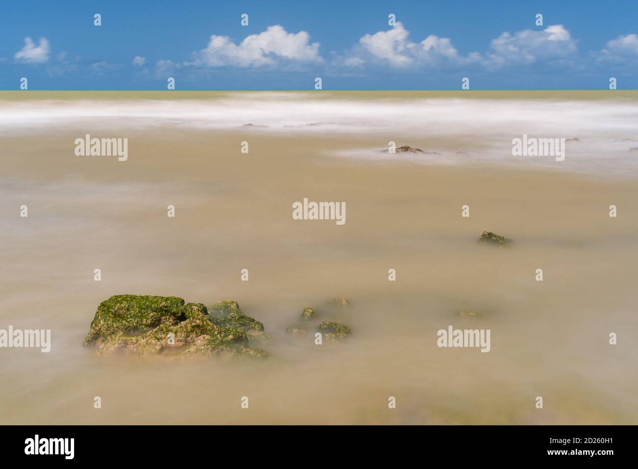 Slime-covered reef emerges from the silky sea and the blue sky of the ...