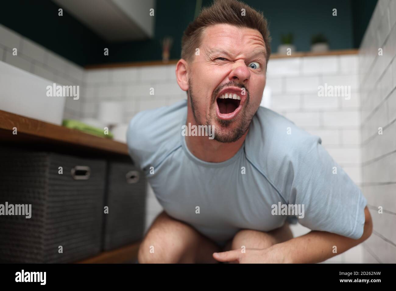 Man sits on toilet with joyful emotions on face and wipes himself with ...