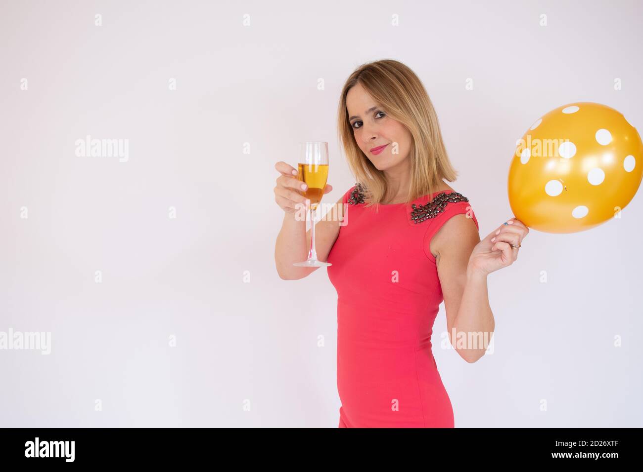 Pretty young woman with gold balloon smiling and drinking champagne ...