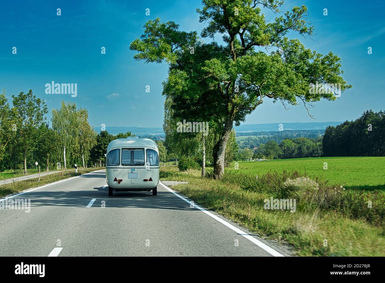 Rear view of an old fashioned mobile home traveling on a country road ...