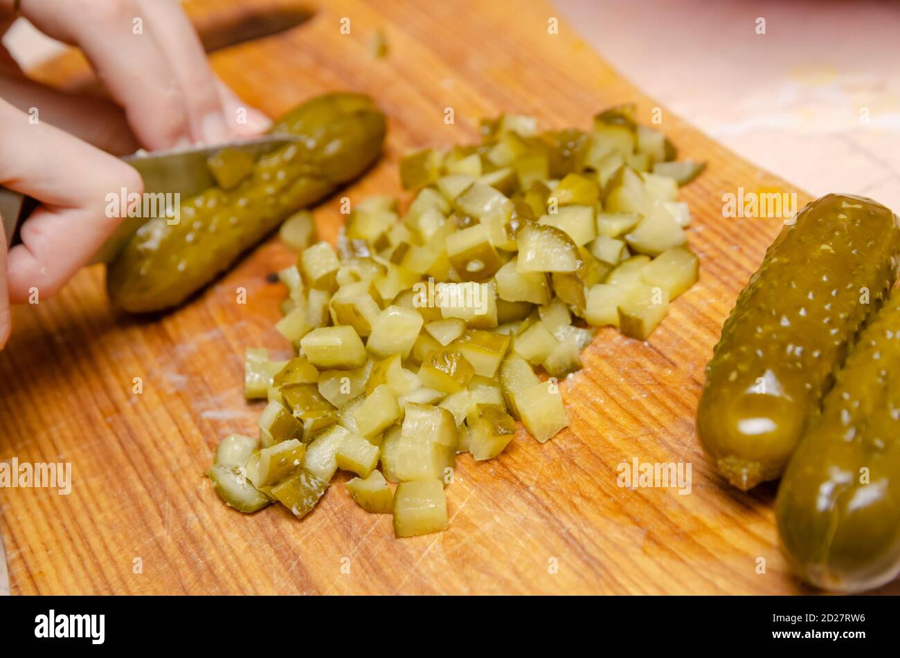 Women's hands cut pickles into cubes on a wooden cutting Board in the ...