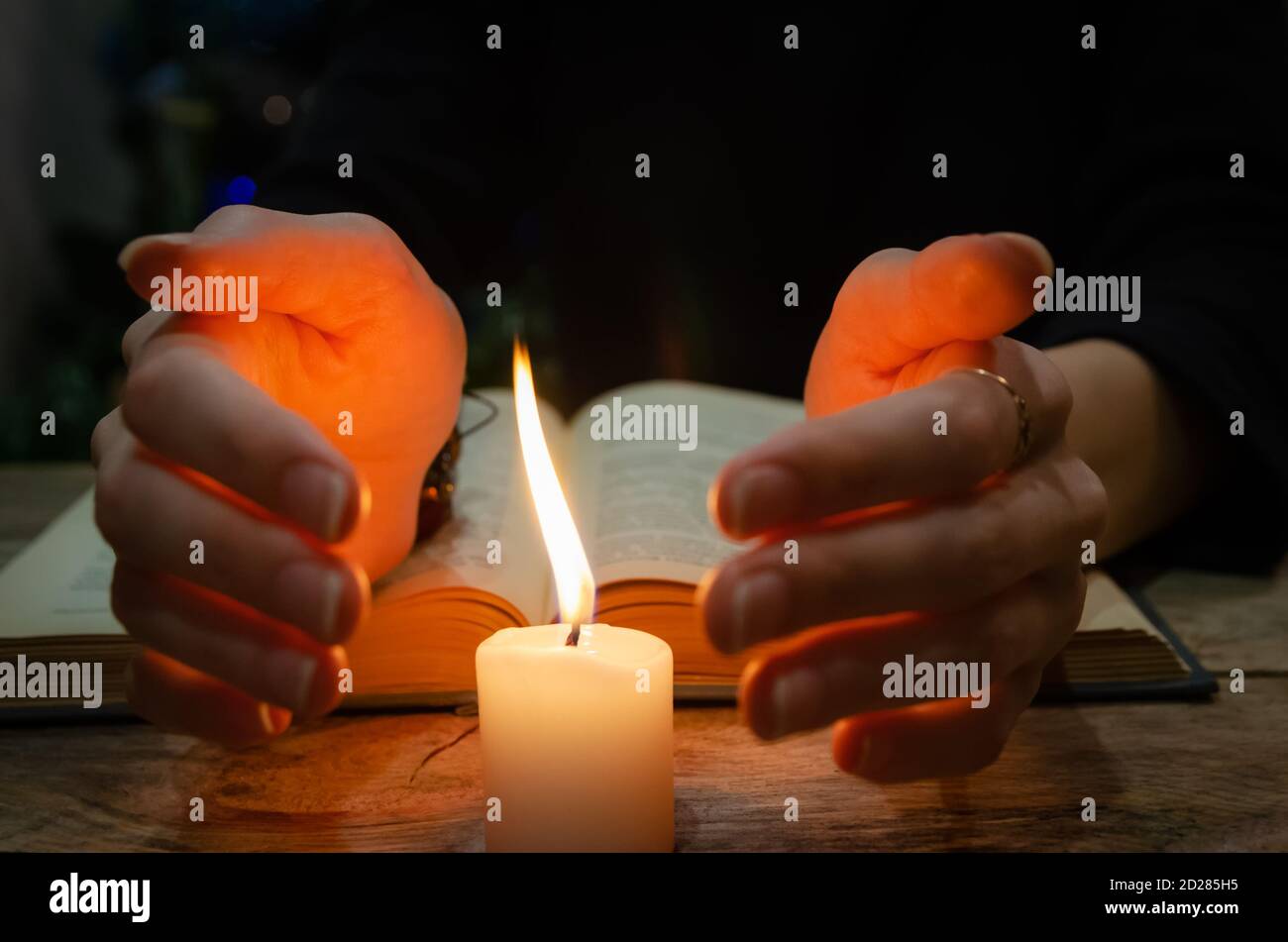 Hands near the candle and a book on the table. Concept of magic ...