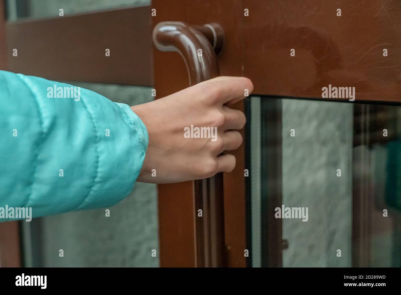Female hand holding the handle of the front door to the building close ...