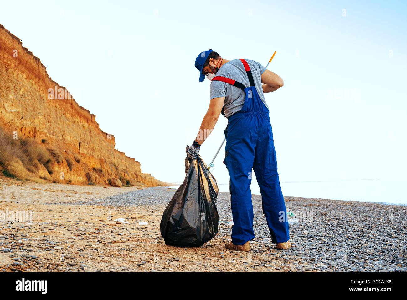Man volunteer collecting garbage on the beach with a reach extender ...