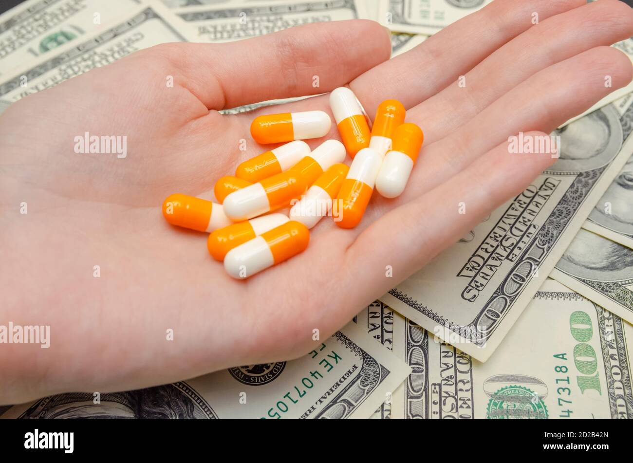 Orange and white pills in hand against the background of dollars. Lots ...