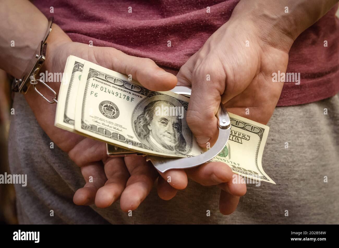 Men's hands in handcuffs behind their backs, holding dollars. concept ...
