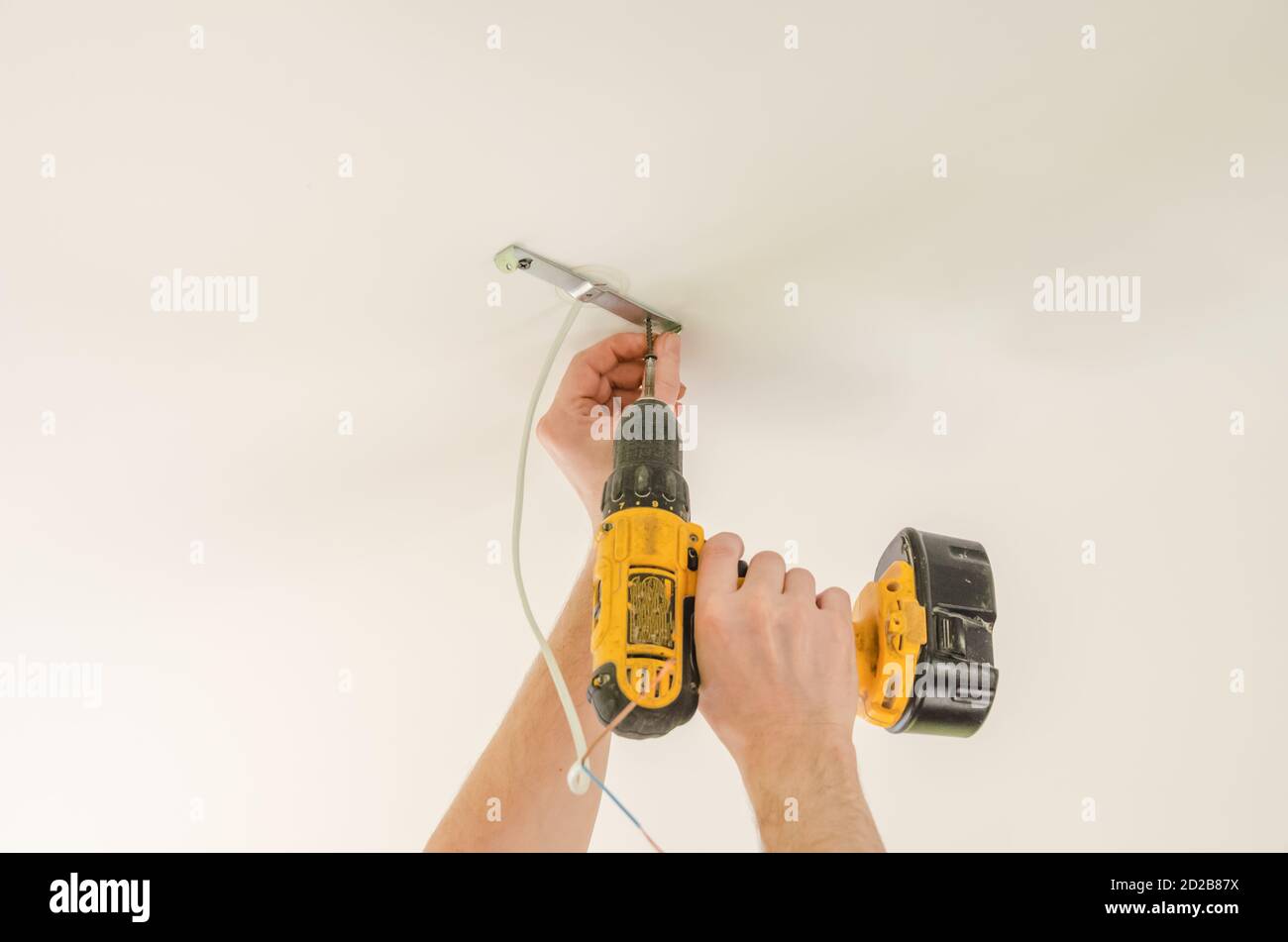 repairman installs a platform under a lamp for a stretch ceiling close ...