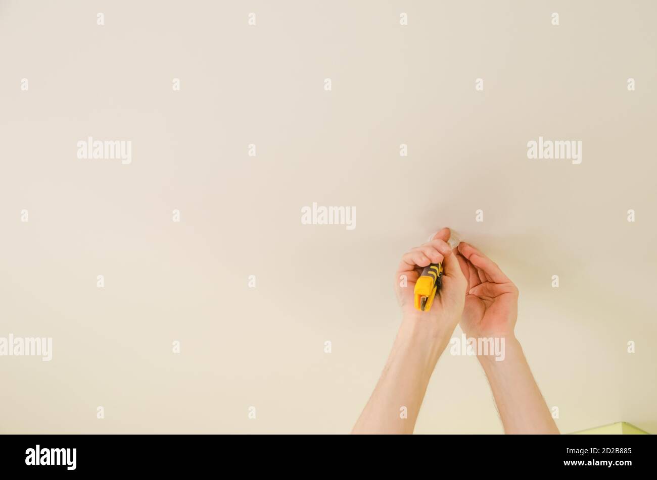 Men's hands cut a hole for a recessed spotlight in a suspended ceiling ...