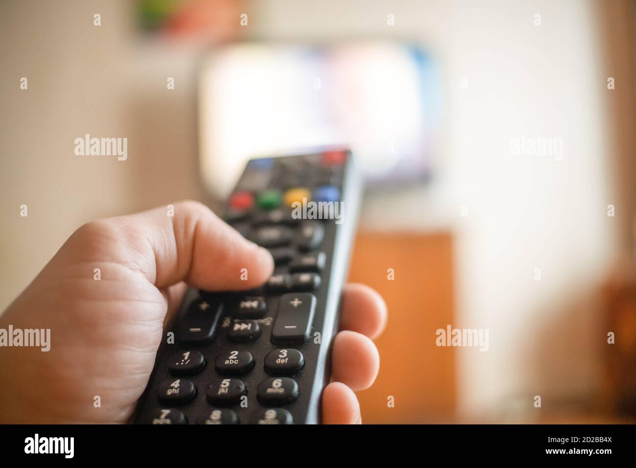 man's hand with the remote is pointed at the TV. Focus on the hand with ...