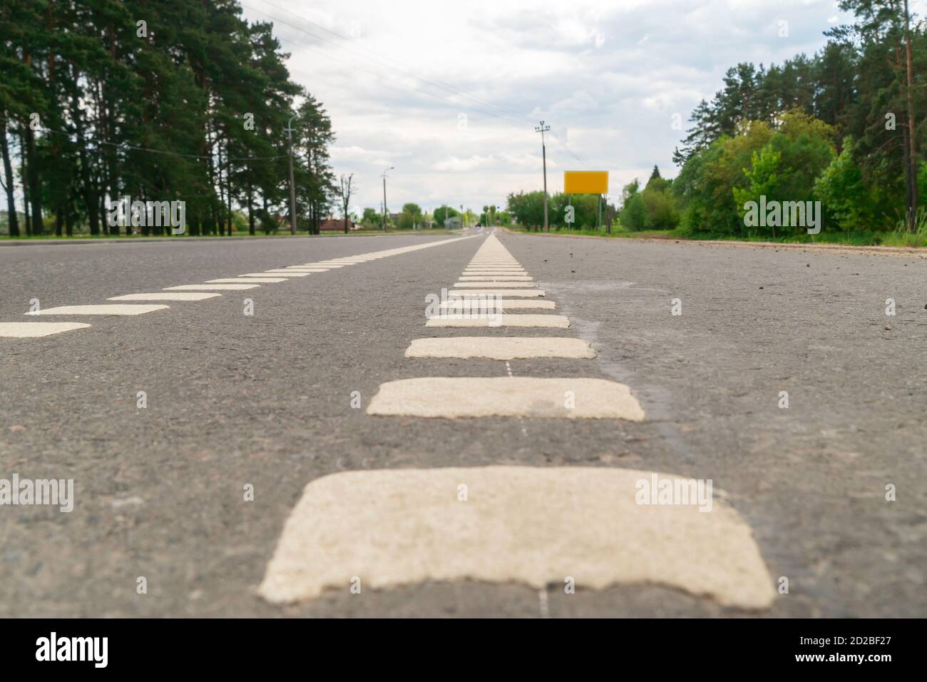 White broken lines of road markings, road sign, trees on the edges of ...