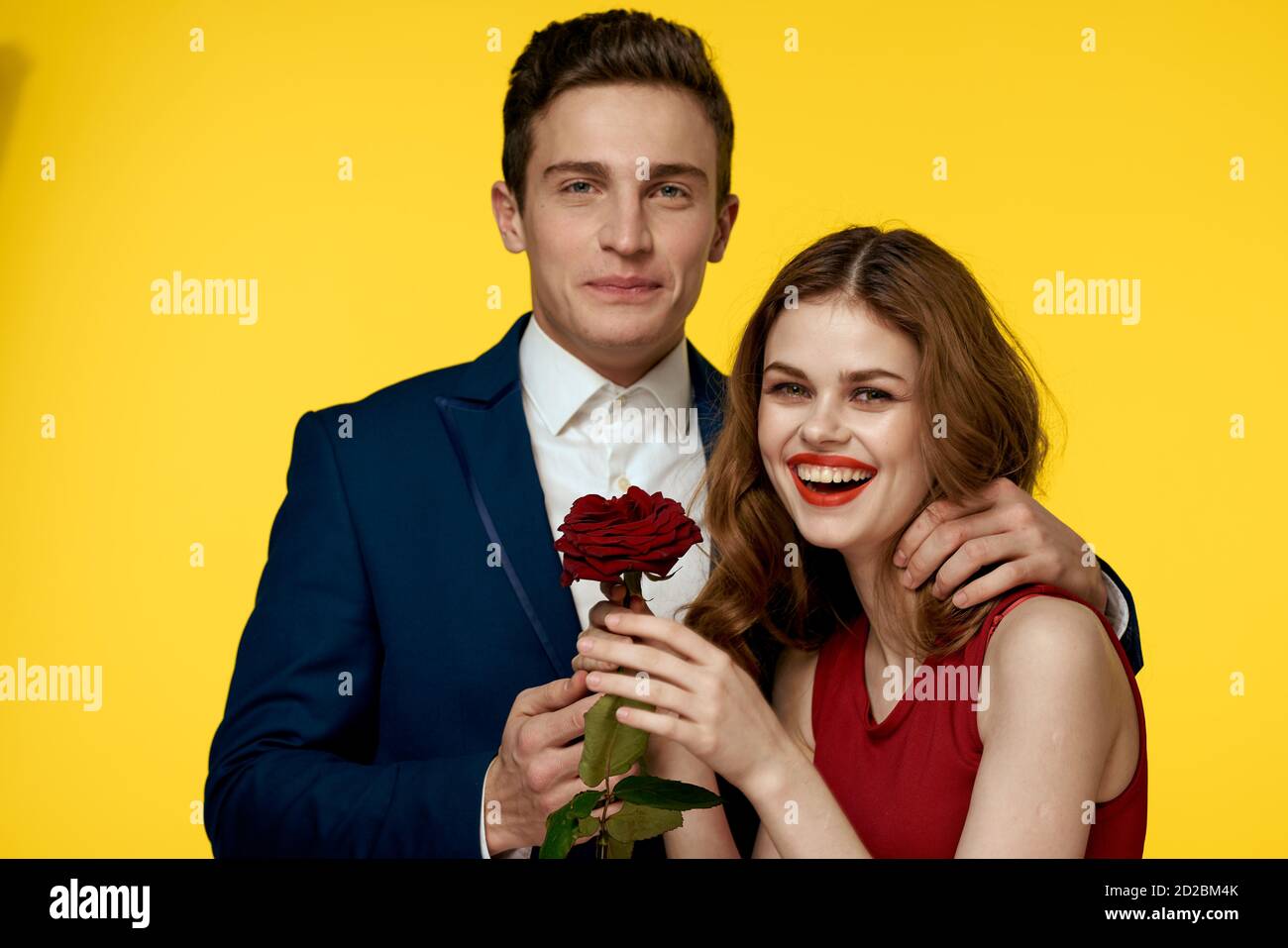 lovers man and woman with a red rose in their hands hugging on a yellow ...