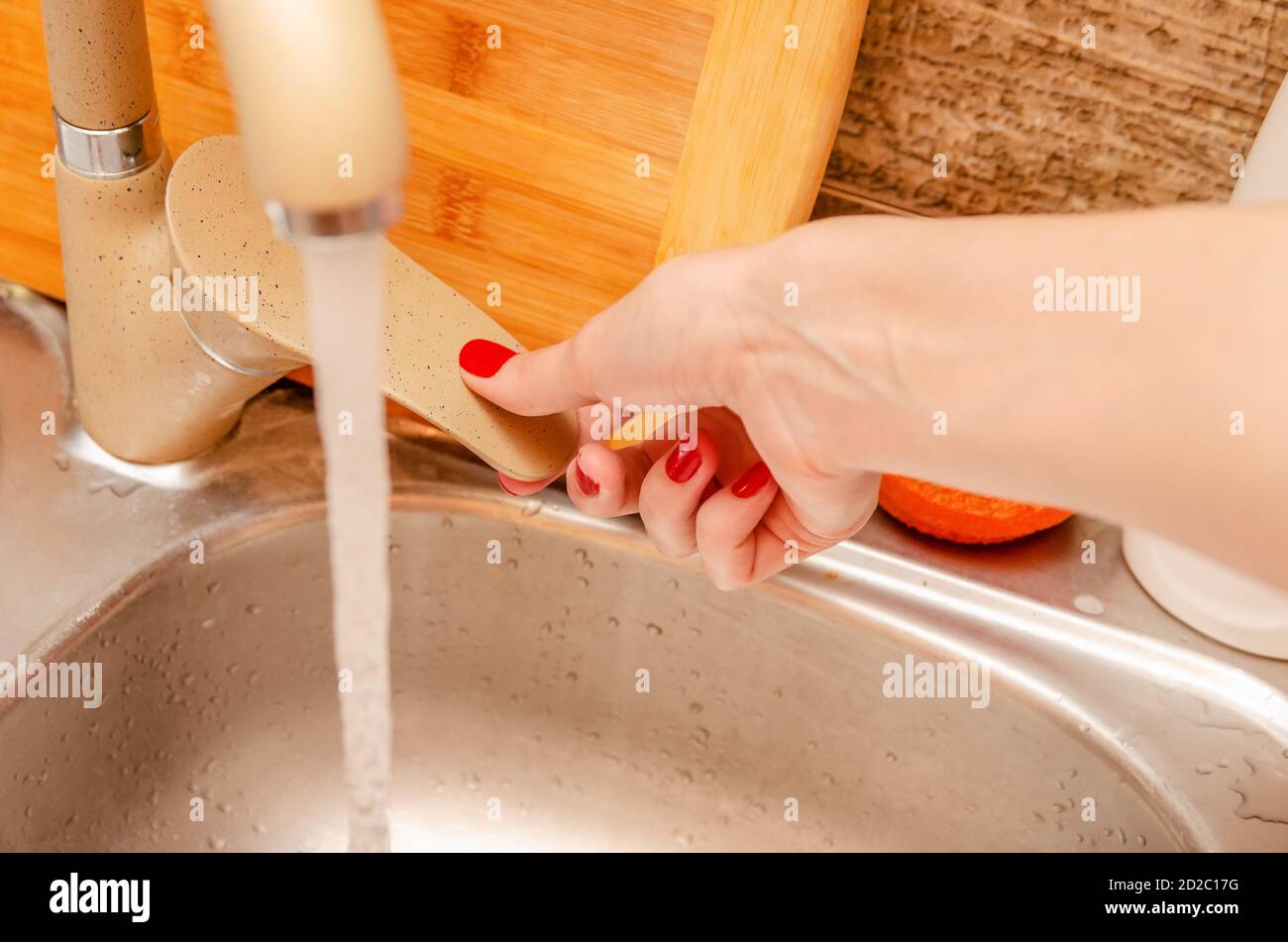 womens brown hand opens the tap in the kitchen close-up, flowing water ...