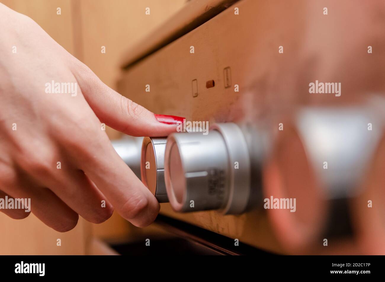 A woman's hand with red nail Polish lights a gray kitchen gas stove ...