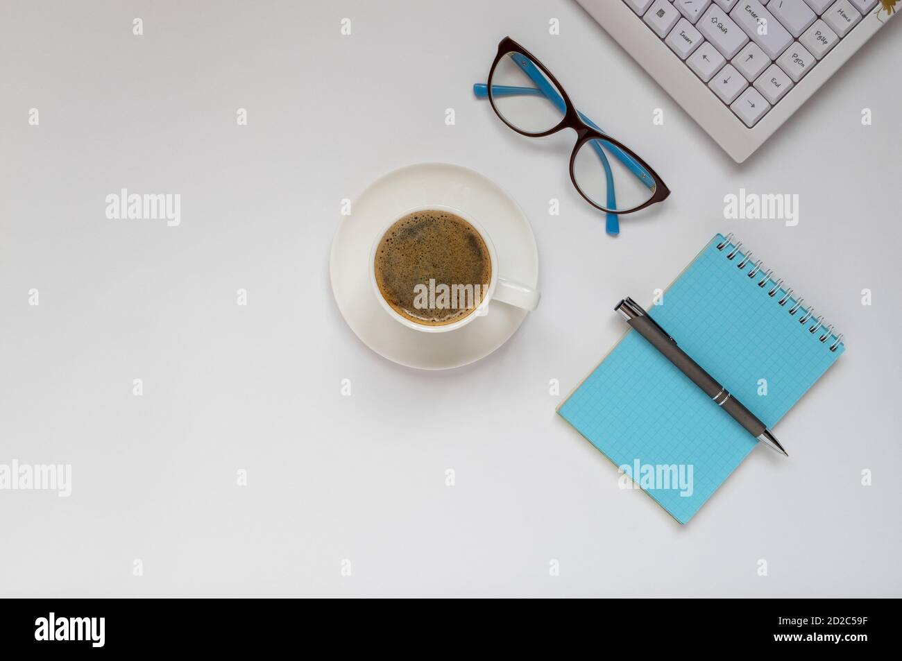 Computer keyboard, a cap of coffee, glasses, notepad and pen on a white ...